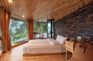Quarto moderno com cama grande, teto de madeira, parede de pedra e vista para o verde.