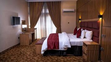 Quarto de hotel com uma cama grande, uma escrivaninha de madeira, televisão de tela plana e janela com cortinas.