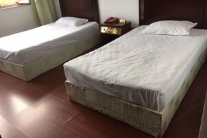 Duas camas de solteiro com lençóis brancos num quarto com soalho de madeira e uma mesa de cabeceira com telefone vermelho.