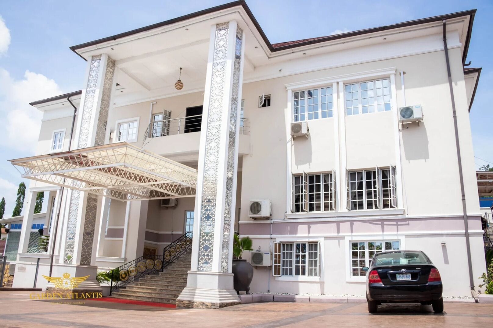 Um edifício de dois andares com entrada coberta, escadaria e um carro estacionado na frente.
