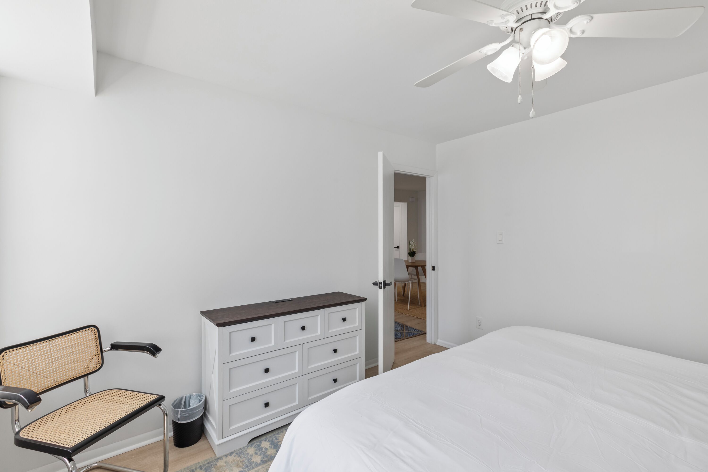 Quarto com cama, cômoda, cadeira e ventilador de teto.