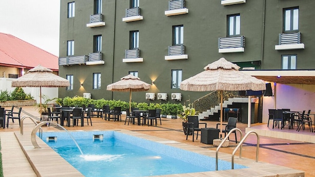 Uma piscina com espreguiçadeiras e guarda-sóis, cercada por um edifício com varandas e aparelhos de ar condicionado.