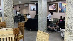 Um restaurante com pilares de mármore, mesas e cadeiras de madeira. Pessoas jantando e uma televisão na parede.