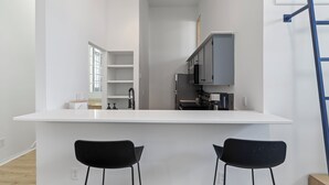 Cozinha moderna com armários brancos, bancada branca e duas cadeiras pretas.