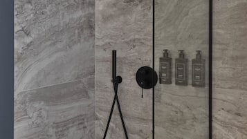 Um chuveiro moderno com um chuveiro de teto, um chuveiro manual e três frascos de shampoo numa prateleira fixada na parede.