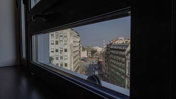 Vista da janela mostrando um horizonte urbano com edifícios altos, céu limpo e rua com veículos.