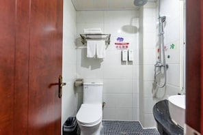 Casa de banho pequena e compacta com sanita, lavatório, chuveiro e um contentor de lixo.