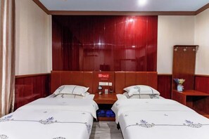 Quarto de hotel com duas camas, uma cabeceira de madeira, uma mesinha de cabeceira e uma pequena mesa com um vaso.