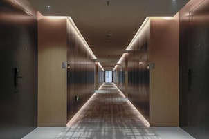 Corredor comprido e estreito, com portas em ambos os lados, que conduz a uma área bem iluminada ao final.