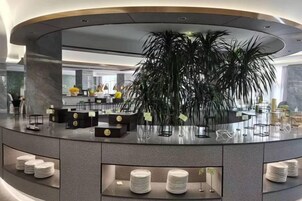 Uma área de recepção moderna com balcão curvo, uma planta grande em vaso e pratos brancos organizados.
