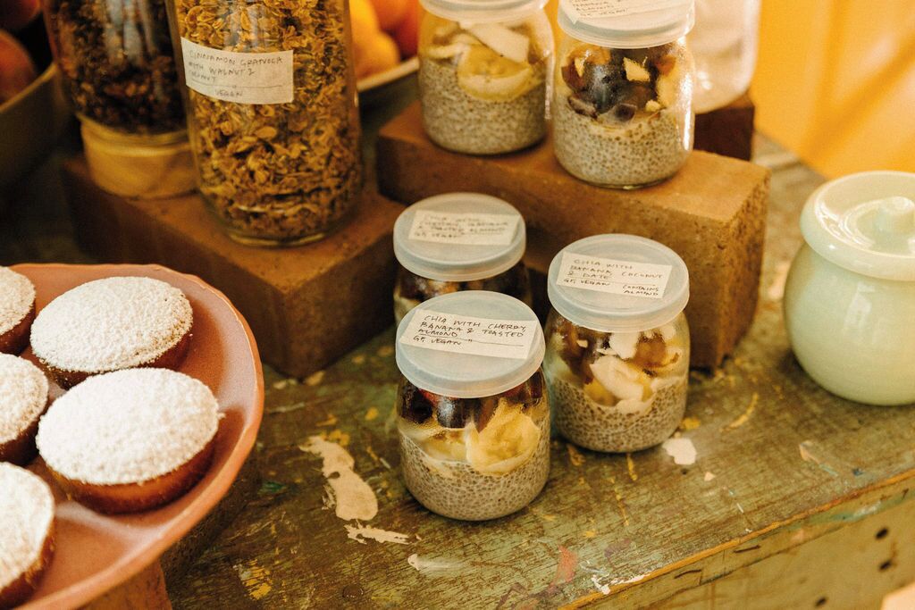 Potes de misturas de sementes de chia sobre blocos de madeira, uma travessa com cupcakes e um jarro de cerâmica branca.