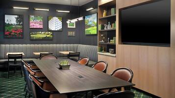 Uma sala de conferência com uma mesa comprida, cadeiras, um sofá e uma tela de televisão.