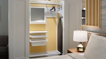 Quarto de hotel com closet espaçoso, cama com cabeceira branca e mesa de cabeceira com luminária.