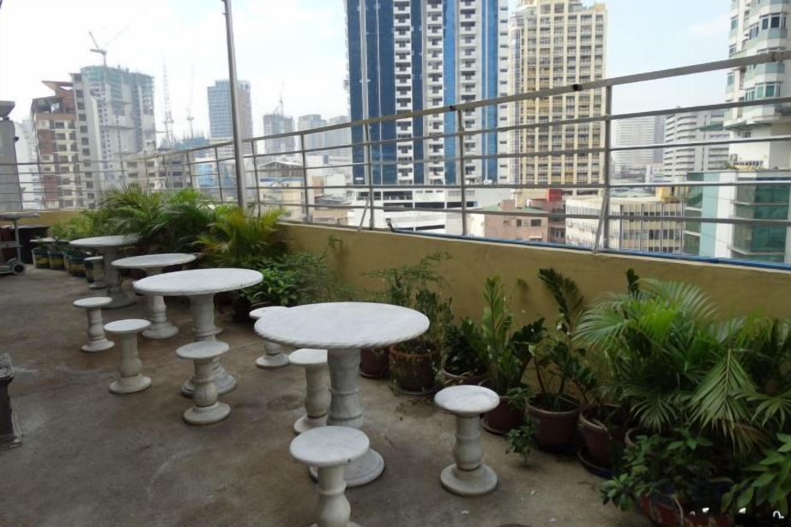 Mobiliário de exterior com mesas e plantas em vasos num terraço com vista para a cidade.