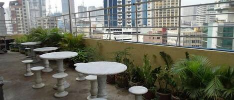 Mobiliário de exterior com mesas e plantas em vasos num terraço com vista para a cidade.