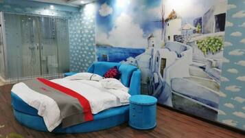 Quarto com cama, uma cadeira azul, mesa de cabeceira azul e box de vidro.