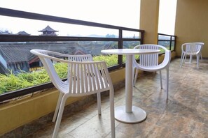Varanda com cadeiras de plástico branco e uma mesa redonda, com vista para um edifício tradicional com telhado de azulejos.