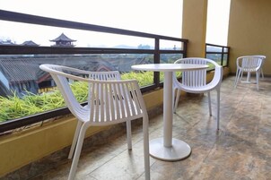 Varanda com cadeiras de plástico branco e uma mesa redonda, com vista para um edifício tradicional com telhado de azulejos.