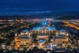 Um edifício grande e tradicional com vários níveis e uma cúpula imponente, rodeado por uma área urbana bem iluminada.