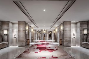 Um saguão moderno de hotel com um longo corredor, paredes de mármore e um tapete vermelho.