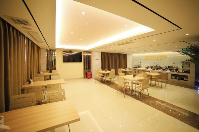 Espaço de refeições de hotel com mesas, cadeiras, um balcão com cardápio e uma tela de televisão.