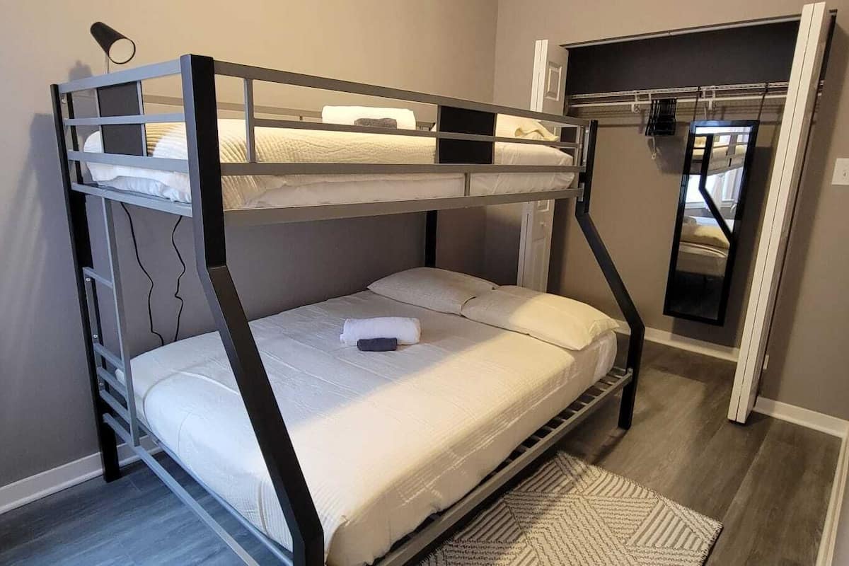 Uma cama beliche com escrivaninha retrátil em quarto com tapete pequeno e espelho na parede.