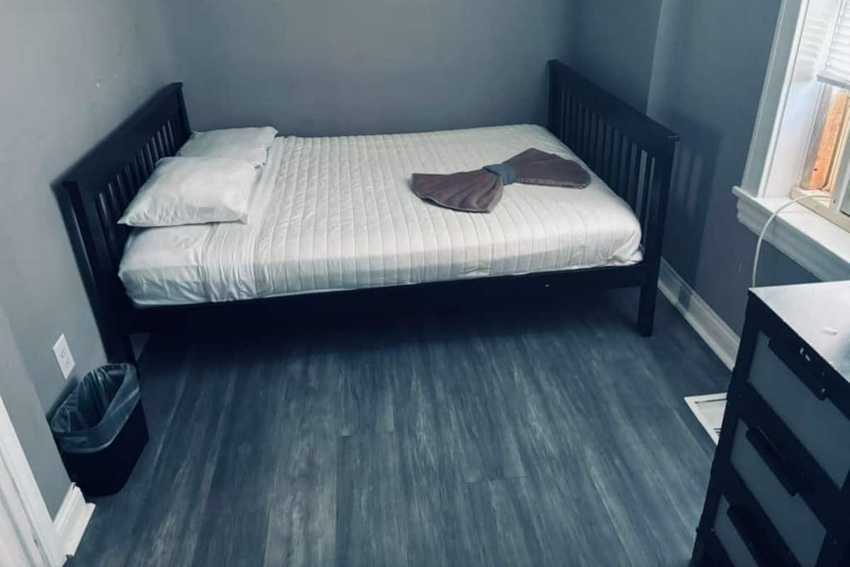 Uma cama de solteiro com cabeceira, mesa de cabeceira e janela com persianas.