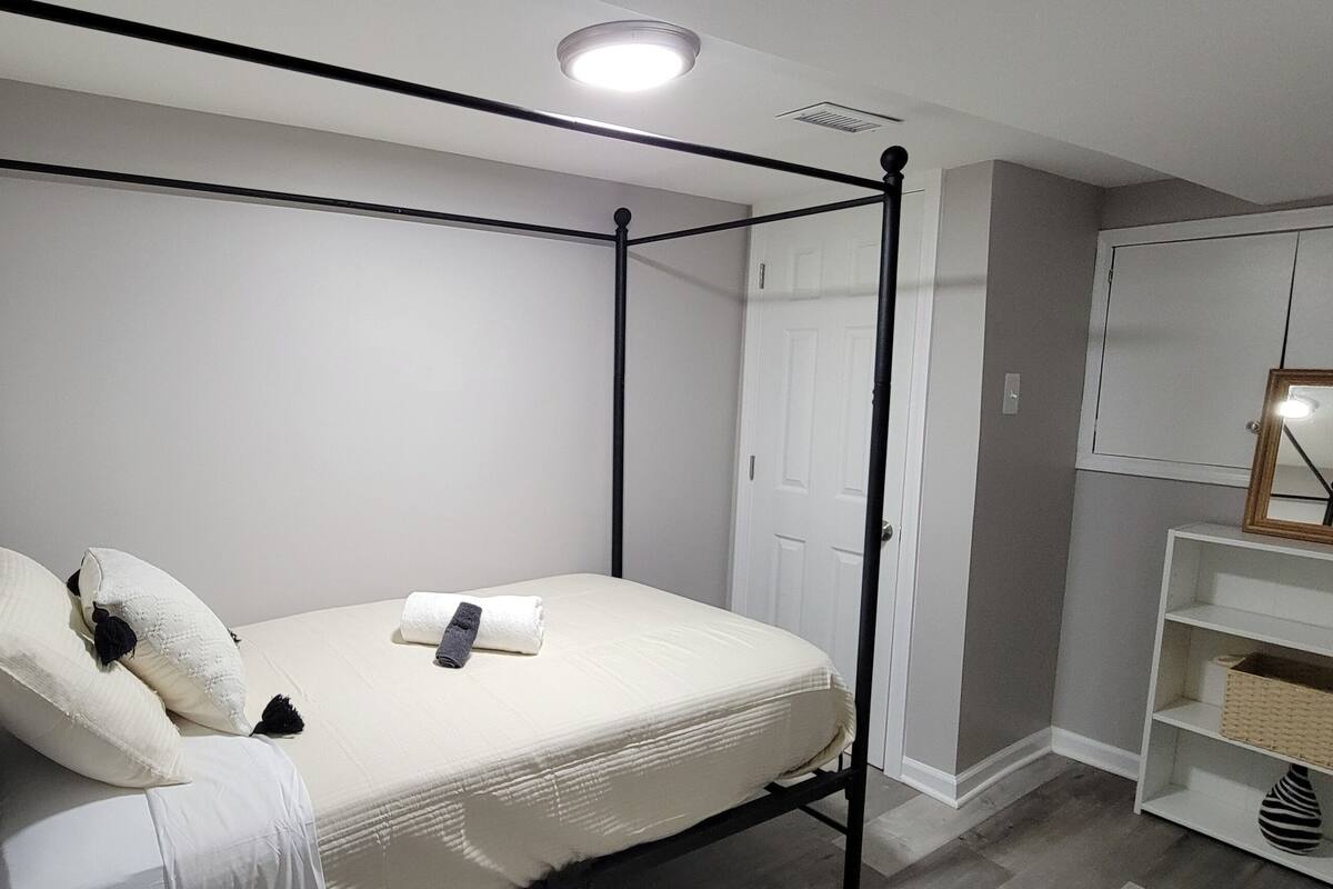Quarto com cama de dossel, paredes brancas, guarda-roupa branco e uma pequena prateleira com espelho e vaso.