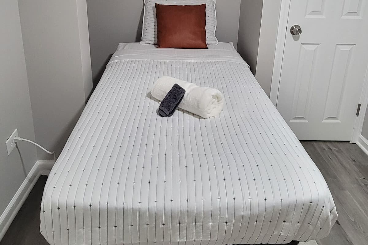 Um quarto com cama, travesseiro, toalha e porta.