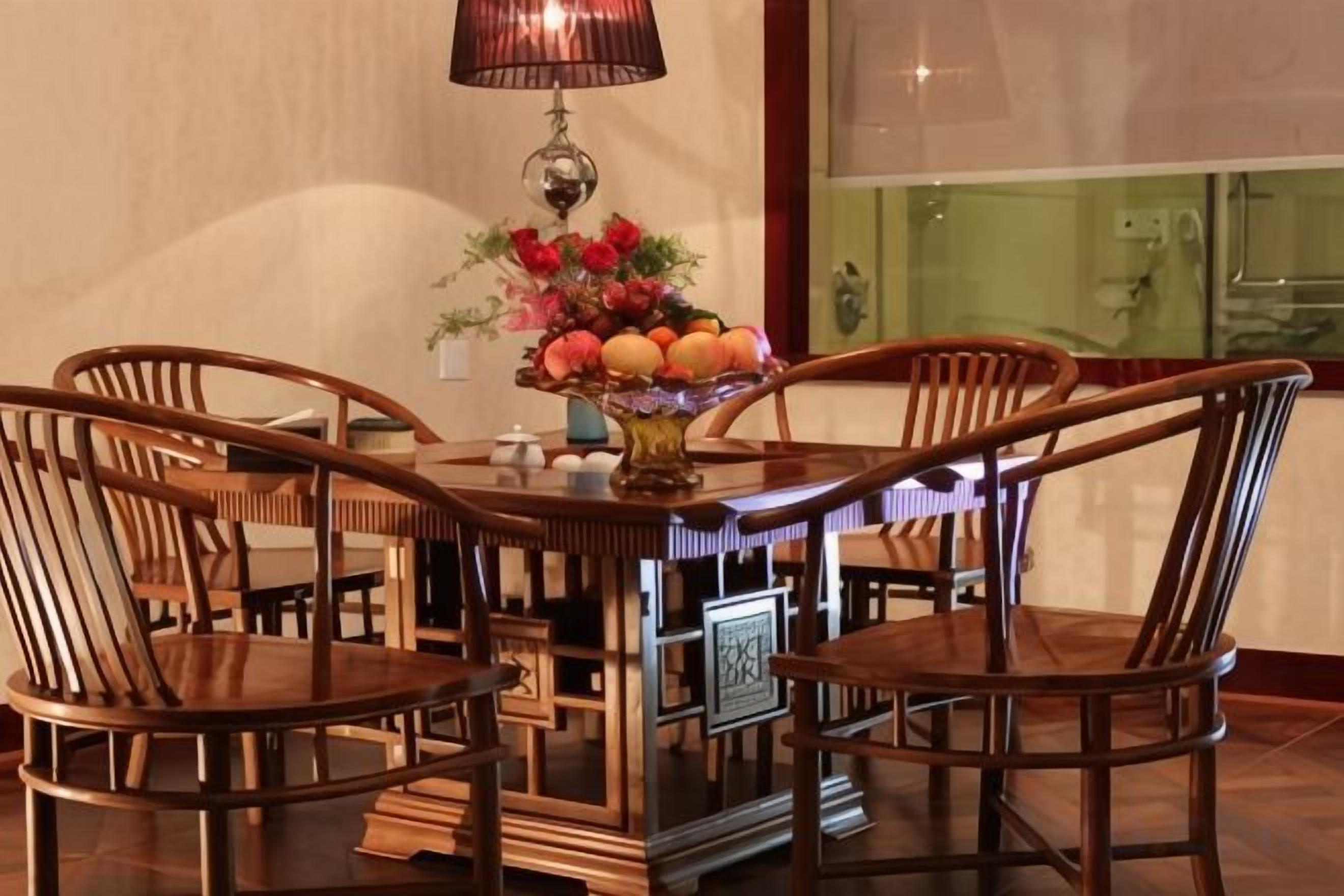 Uma mesa de jantar com quatro cadeiras de madeira, um vaso com flores e um abajur.