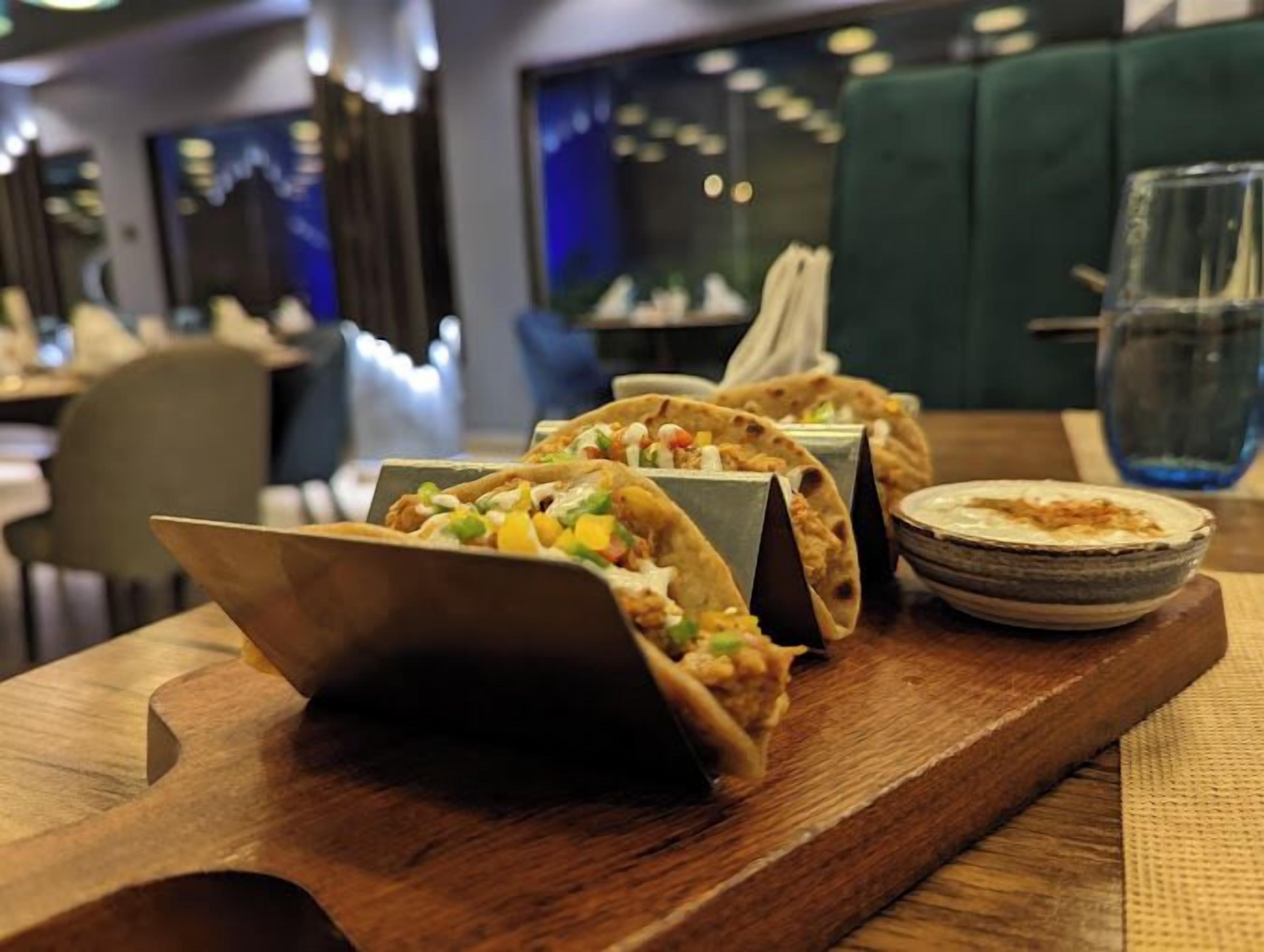 Ambiente de restaurante com uma tábua de madeira que contém tacos e uma tigela de molho.