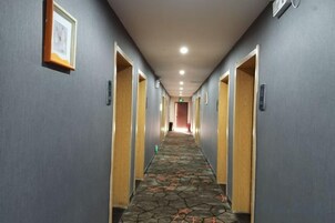 Corredor de hotel com piso coberto por carpete, portas de madeira e quadros decorativos nas paredes.