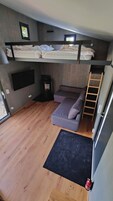 Quarto compacto com cama beliche, sofá, televisão pequena e escada.
