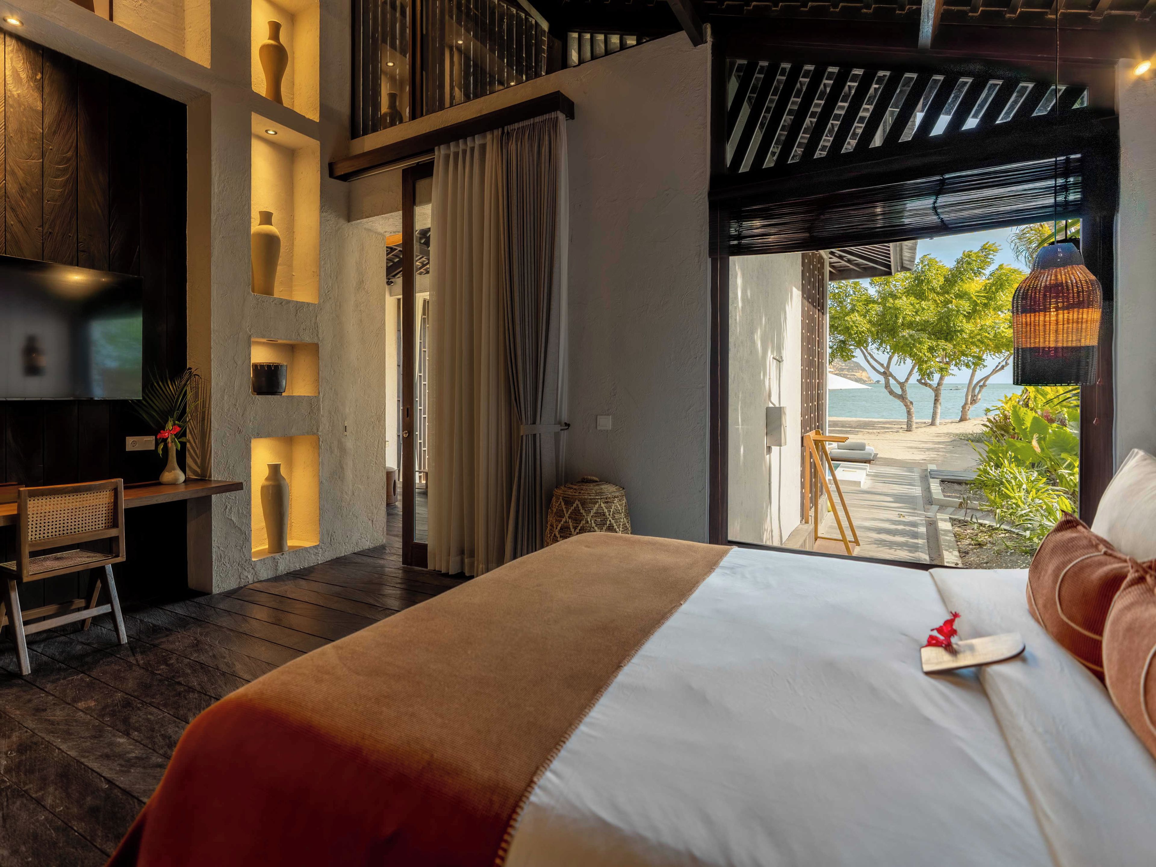 Quarto com cama, escrivaninha e vista para a praia.