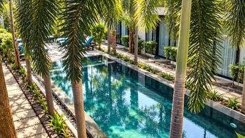 Piscina cercada por palmeiras e área de estar com espreguiçadeiras.