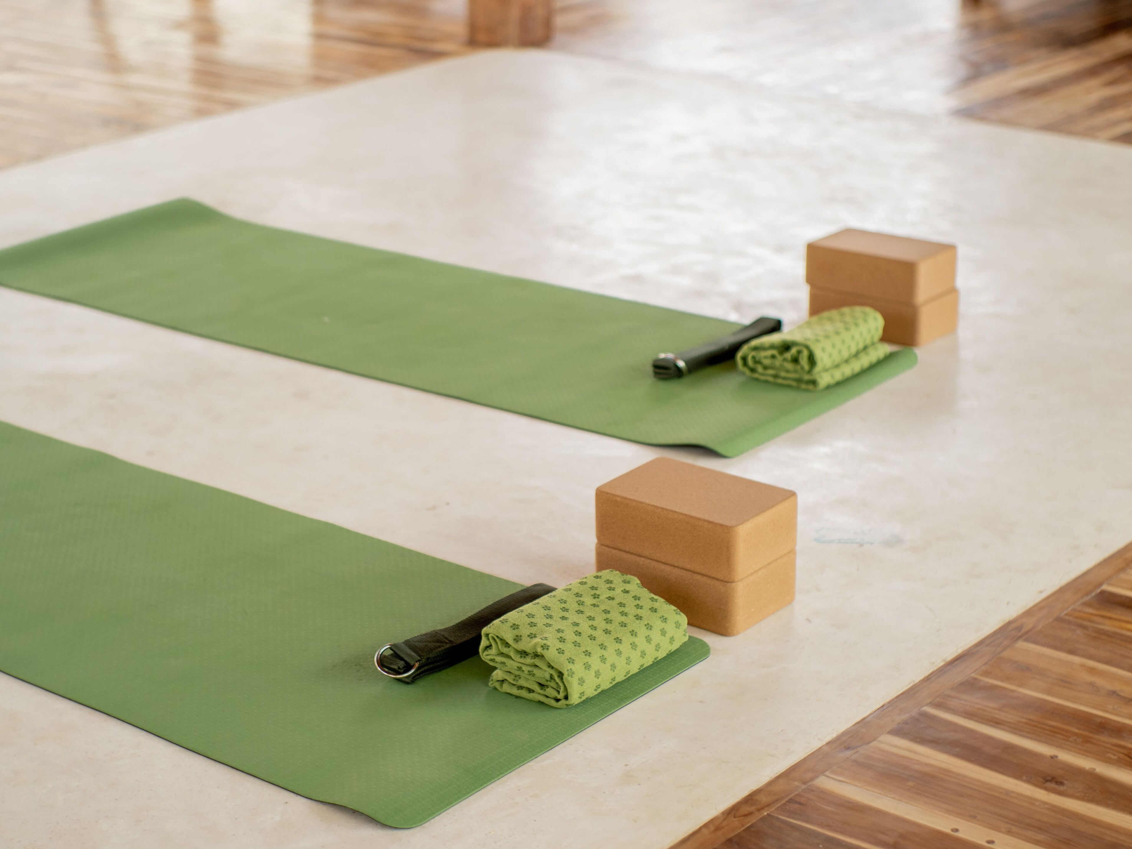 Um quarto com um tapete de yoga verde, um bloco de yoga e uma toalha enrolada em um chão de madeira.