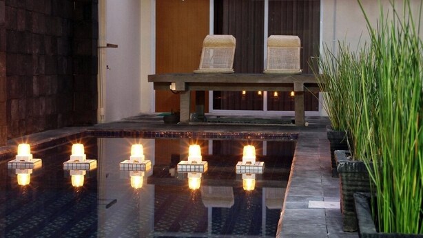 Uma área de piscina com um banco e cadeiras, cercada por vasos de plantas.