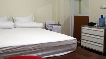 Quarto de hotel com uma cama grande, cômoda de madeira, uma cadeira vermelha e uma garrafa de água sobre a cômoda.
