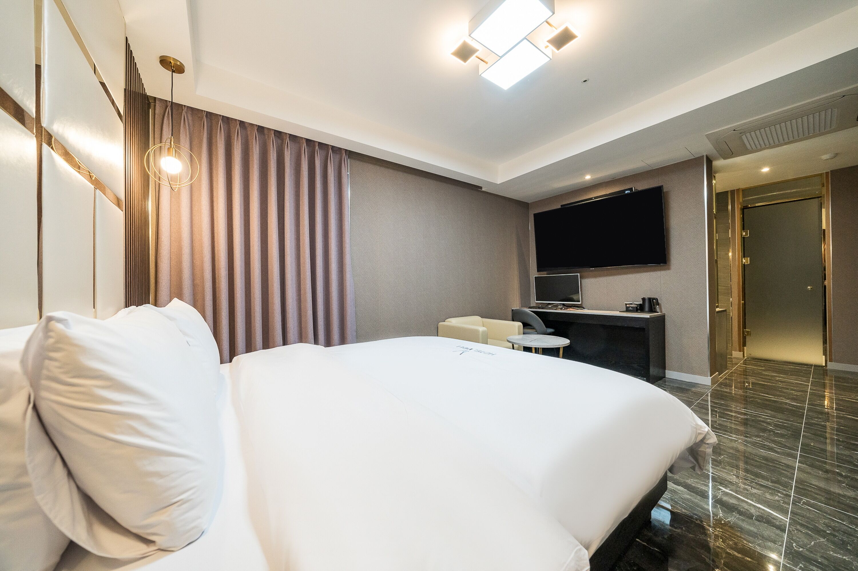 Quarto de hotel com cama grande, escrivaninha, televisão de tela plana e porta que dá para outro cômodo.