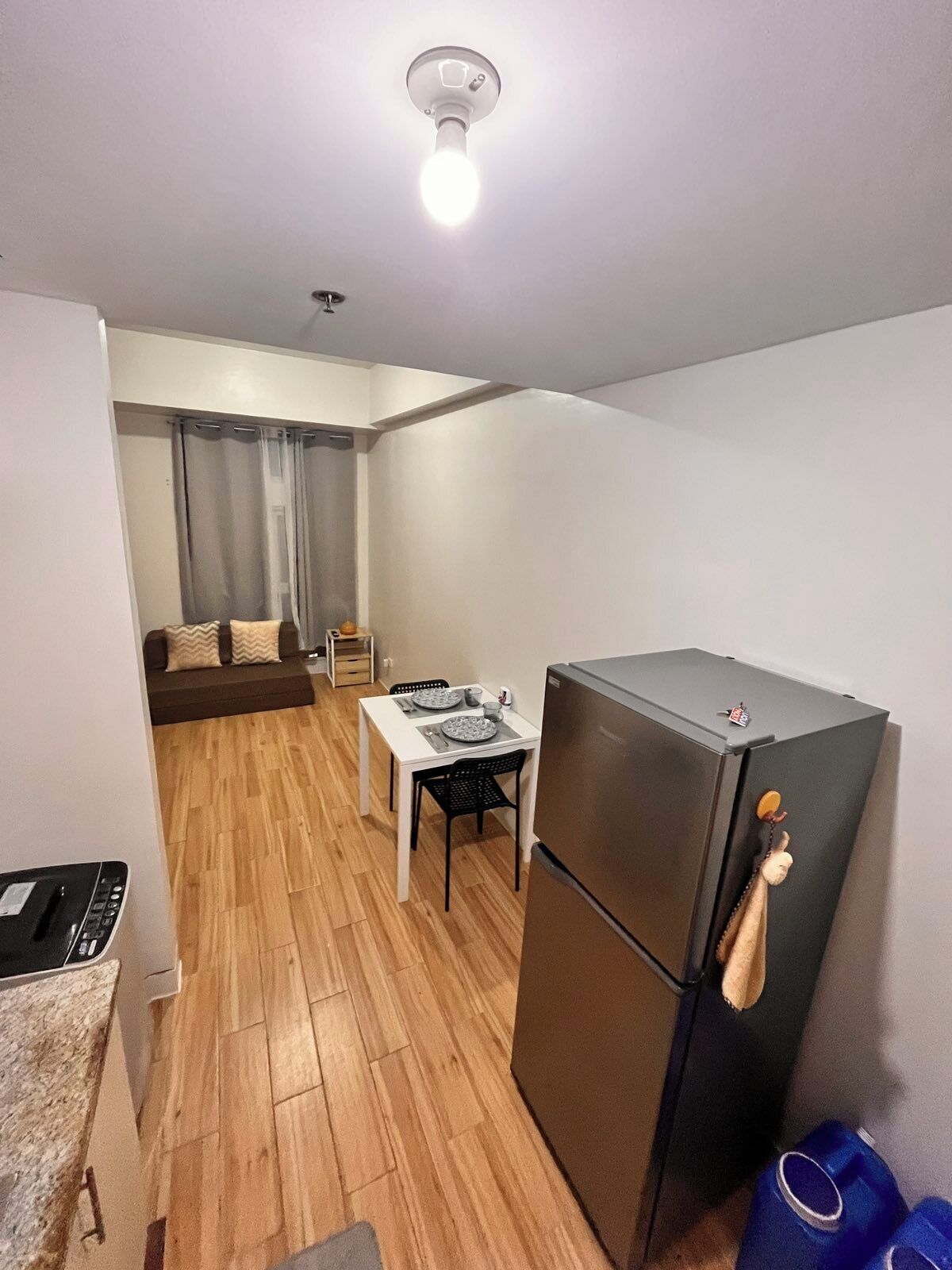 Uma cozinha compacta com geladeira, uma mesa de jantar com cadeiras e um sofá ao fundo.