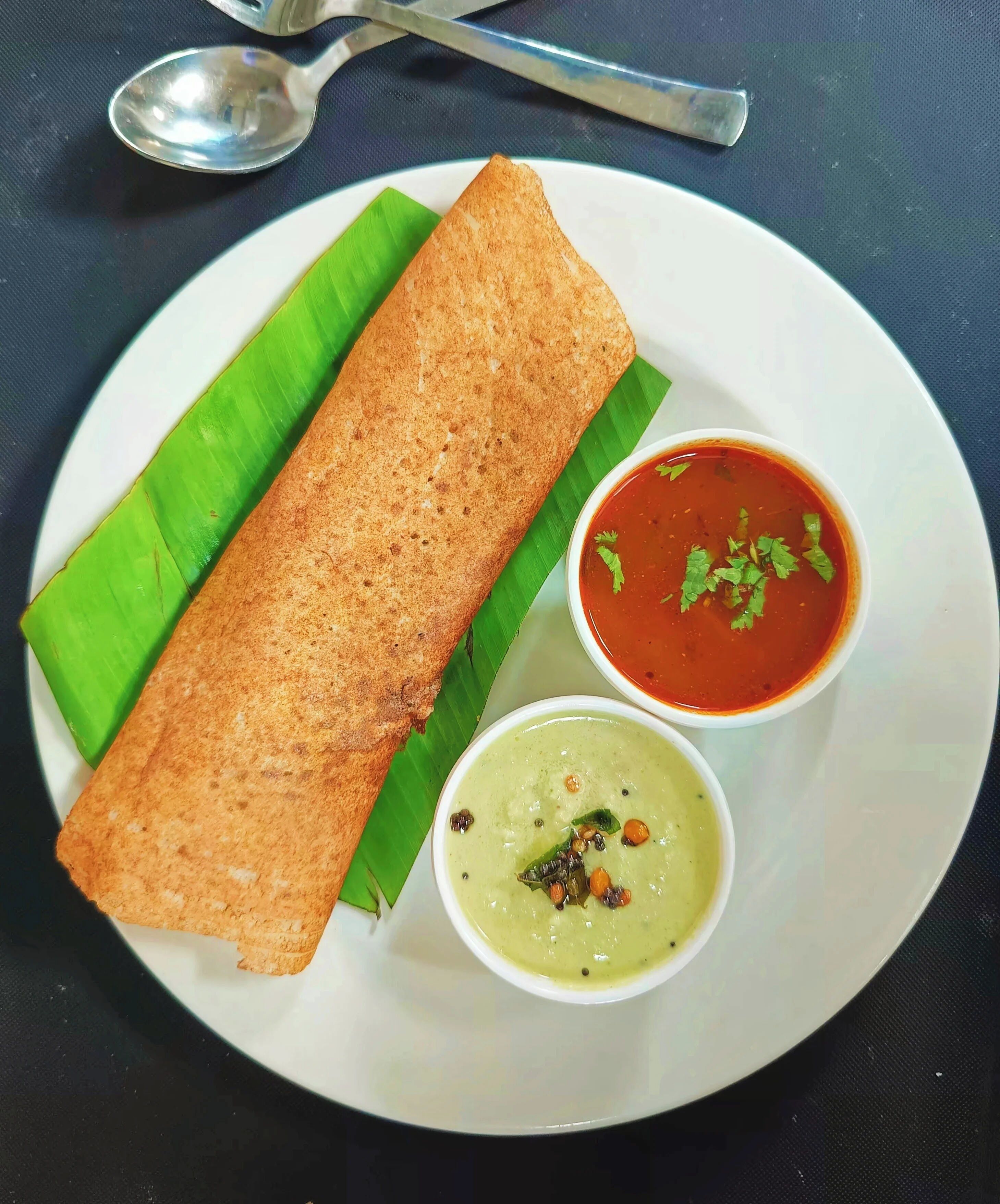 Um prato com um dosa, dois tipos de chutney e uma colher.