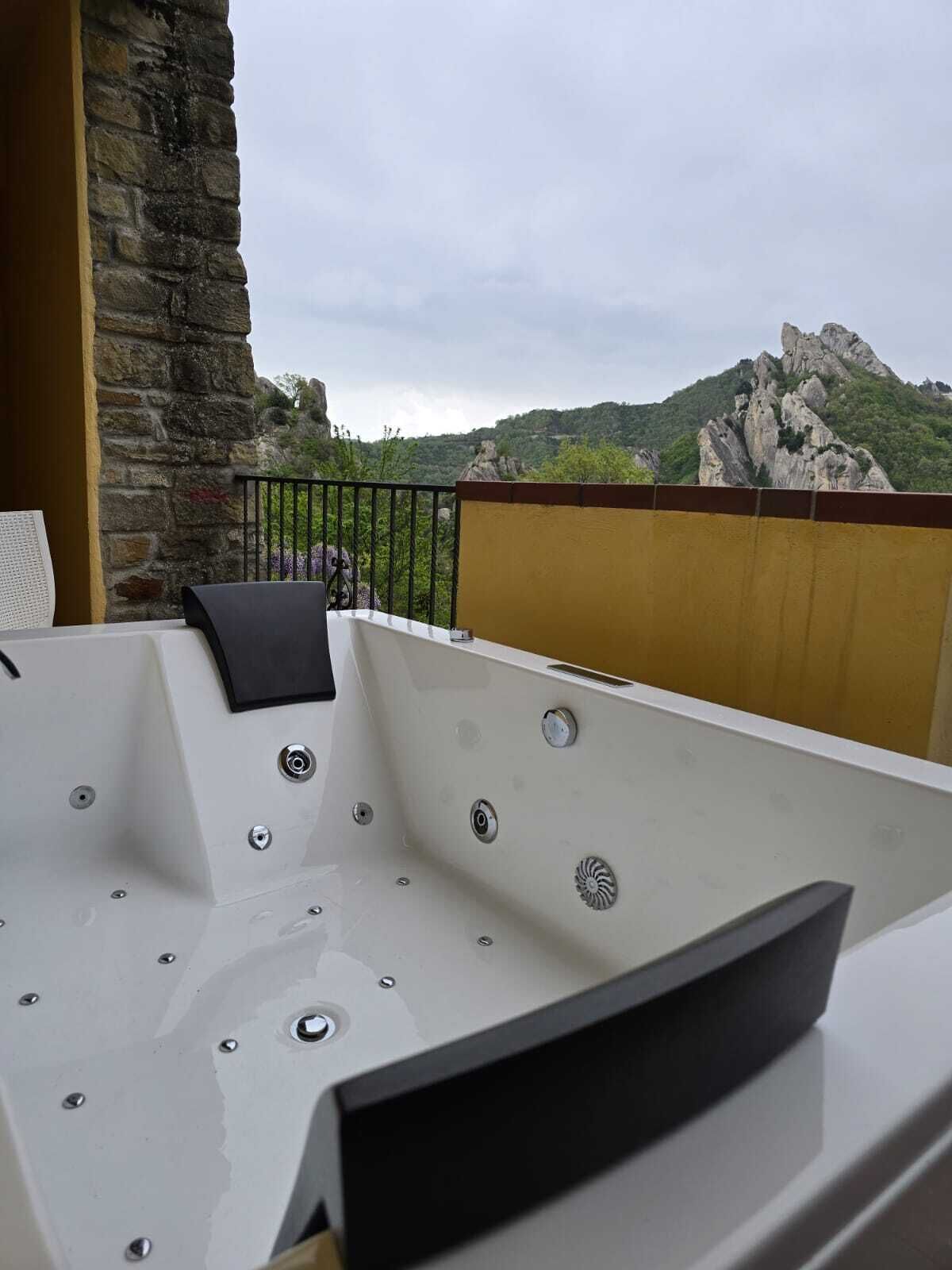 Uma banheira de hidromassagem numa varanda com uma parede de pedra e vista para colinas rochosas.