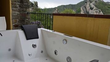 Uma banheira de hidromassagem numa varanda com uma parede de pedra e vista para colinas rochosas.