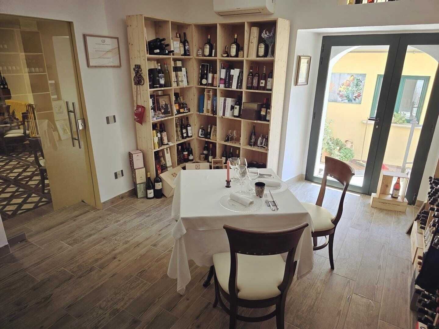 Uma área de refeições com uma mesa posta para dois, rodeada por estantes de madeira cheias de garrafas de vinho.