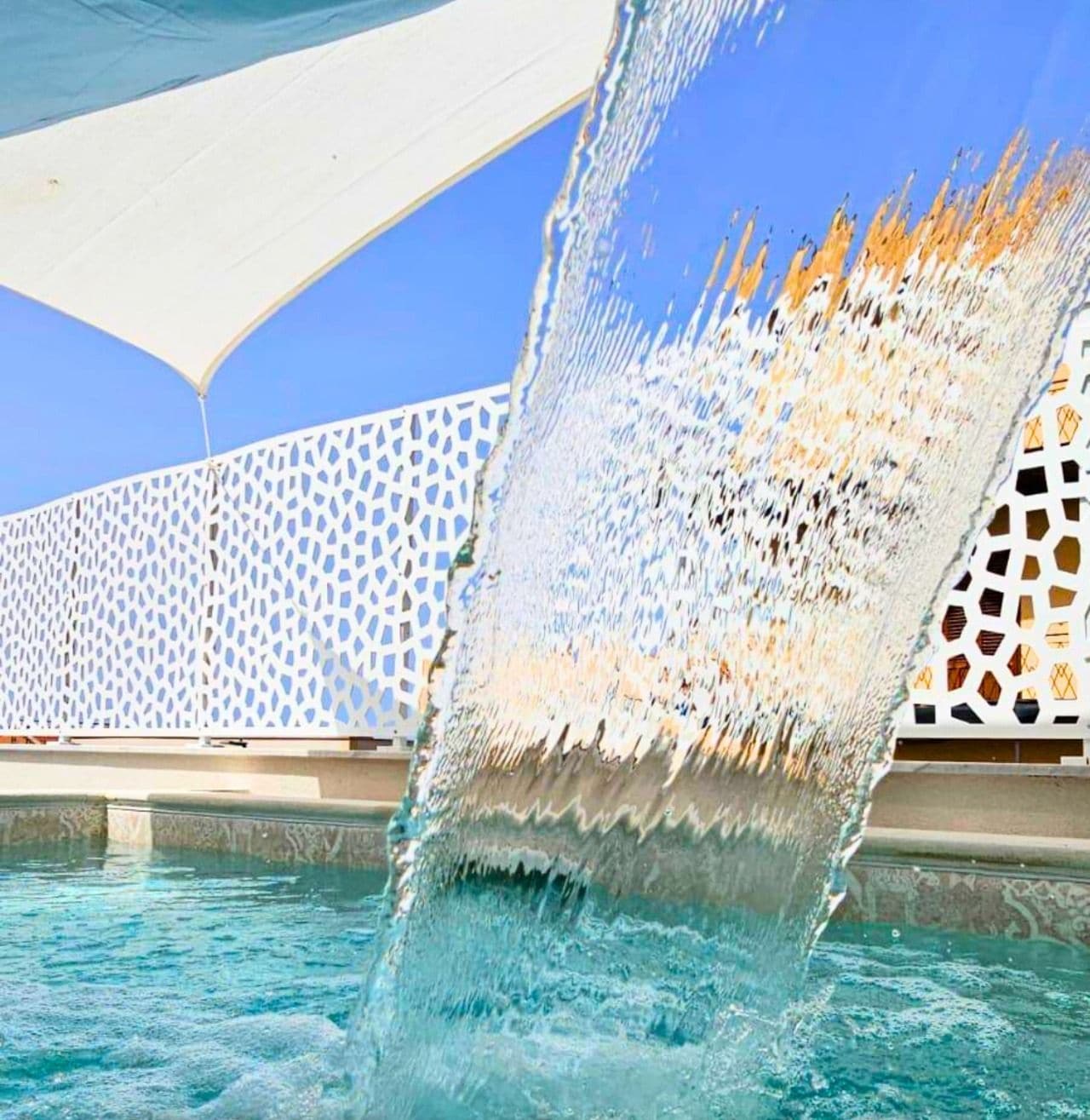 Uma fonte com uma piscina azul límpida e uma cerca branca e geométrica ao fundo.
