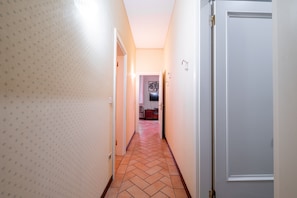 Um corredor com papel de parede estampado, piso ladrilhado e uma porta fechada.