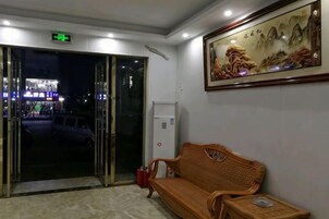 Um saguão de hotel com balcão de recepção, um sofá, um quadro na parede e uma porta que dá para o exterior.