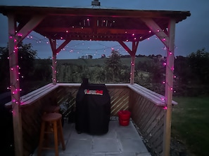 Um gazebo com churrasqueira, luzes de fada e vista para a paisagem.