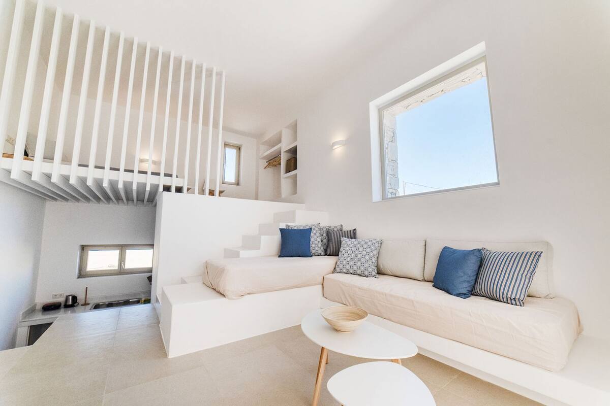 Um interior moderno com design minimalista, apresentando uma escada, um conjunto de sofás e uma pequena mesa redonda.