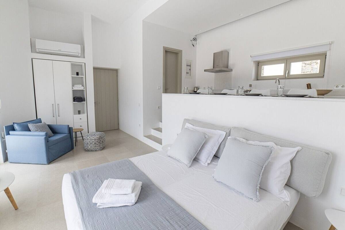 Quarto moderno com uma cama grande, um sofá azul, um guarda-roupa e uma área de cozinha com janela.